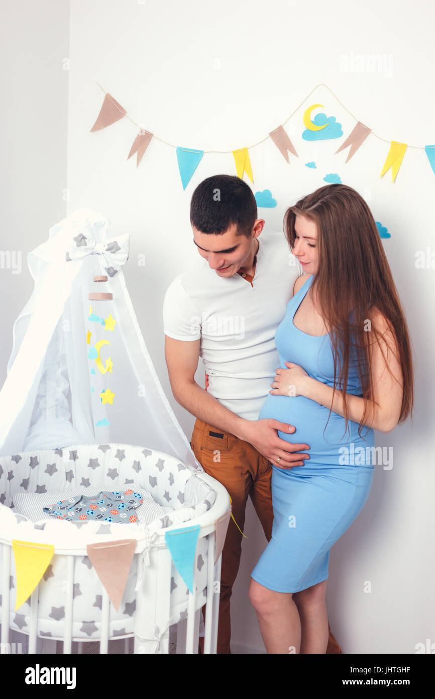 Happy young expecting couple in love standing near a new baby crib ...