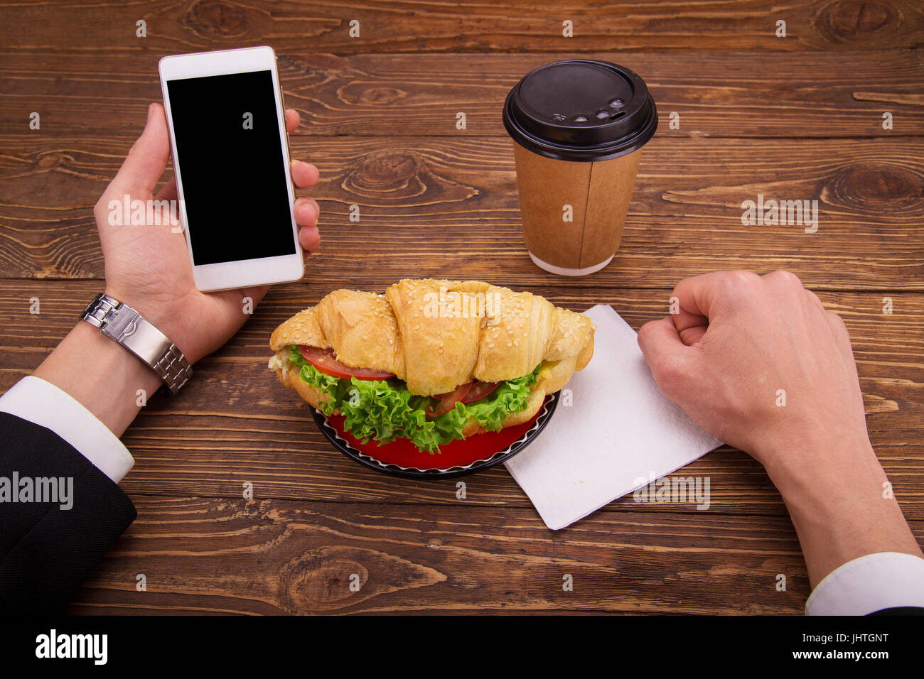 Croissant sandwich on a saucer, mobile phone in hand.Coffee on the ...