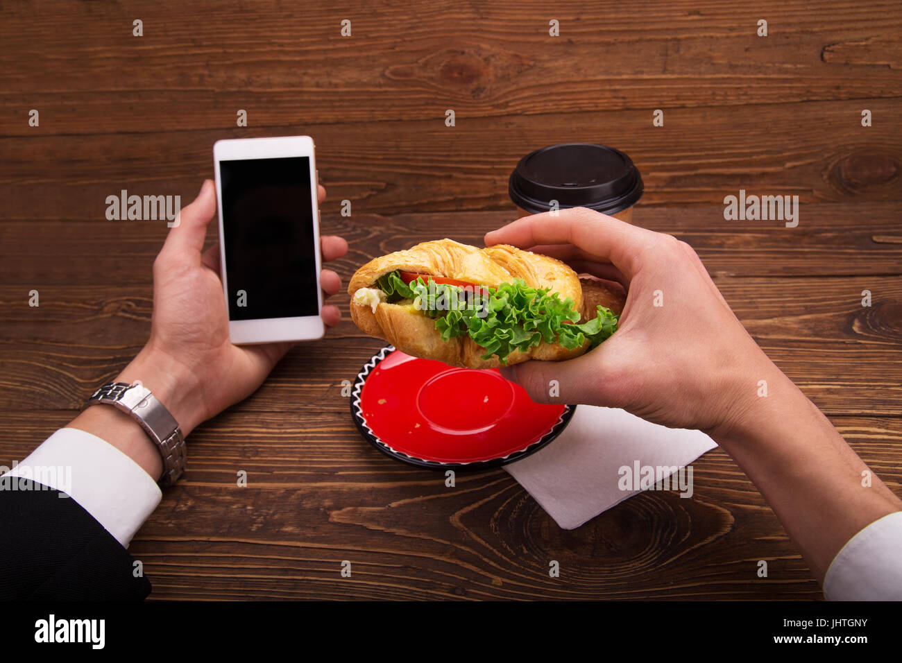 Croissant sandwich and mobile phone in hand. Business lunch concept ...
