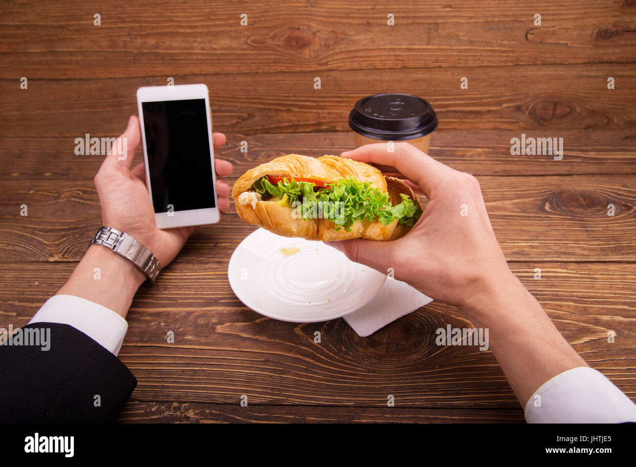 Croissant sandwich and mobile phone in hand. Business lunch concept ...
