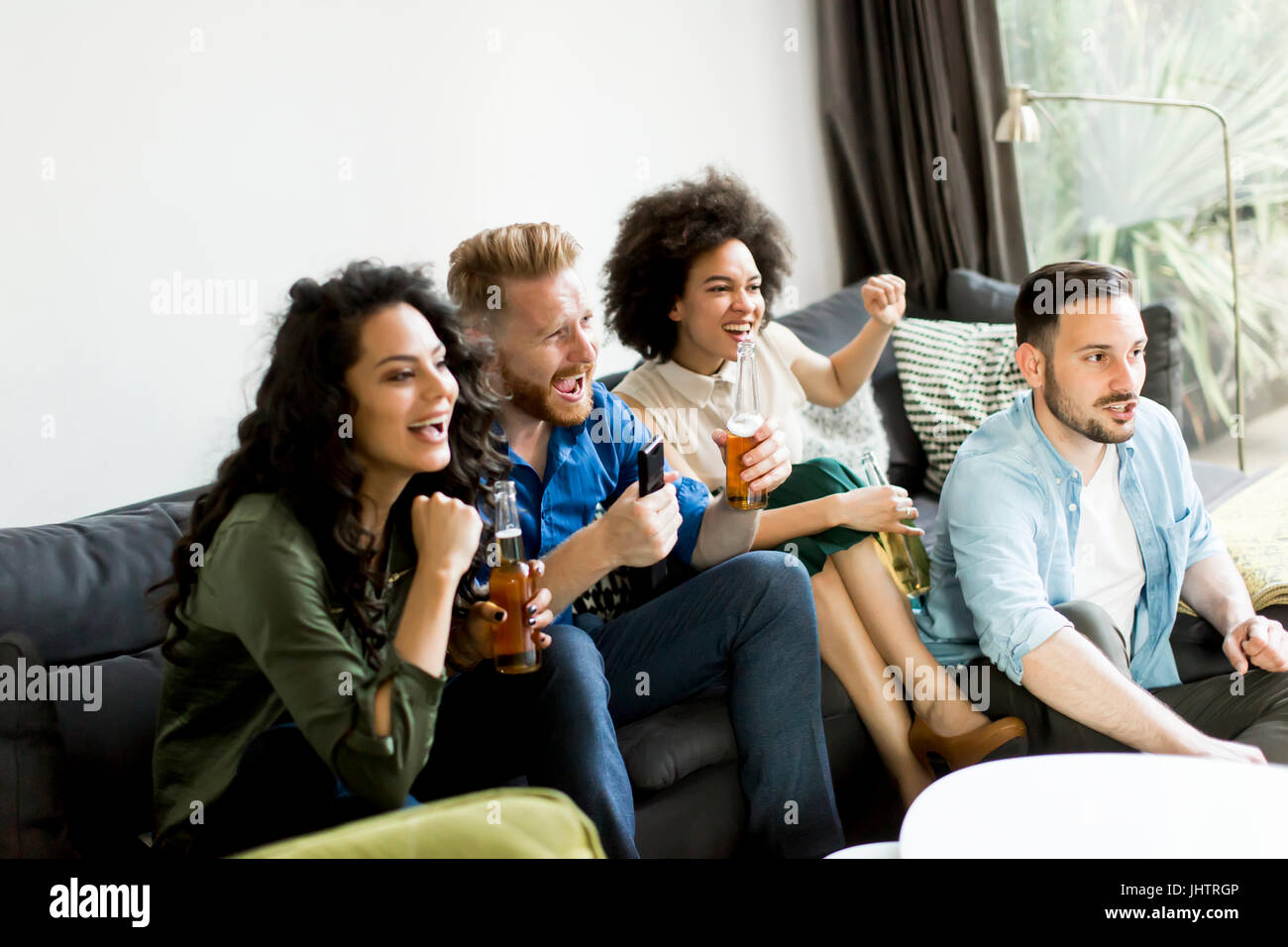 Group of friends watching TV , drinking cider and having fun in the ...