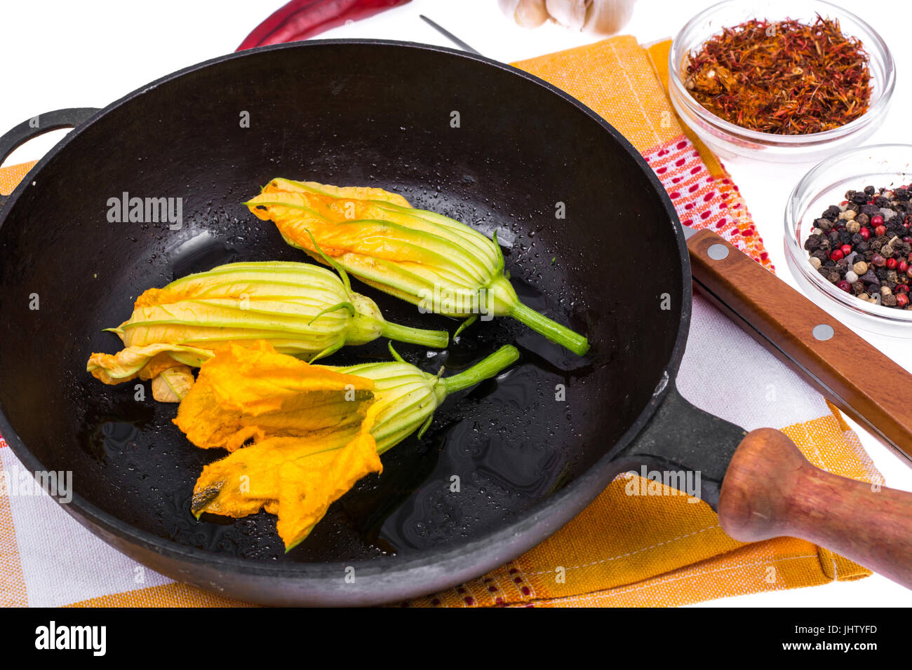 Yellow pumpkin flowers and zucchini in frying pan for cooking. Studio ...