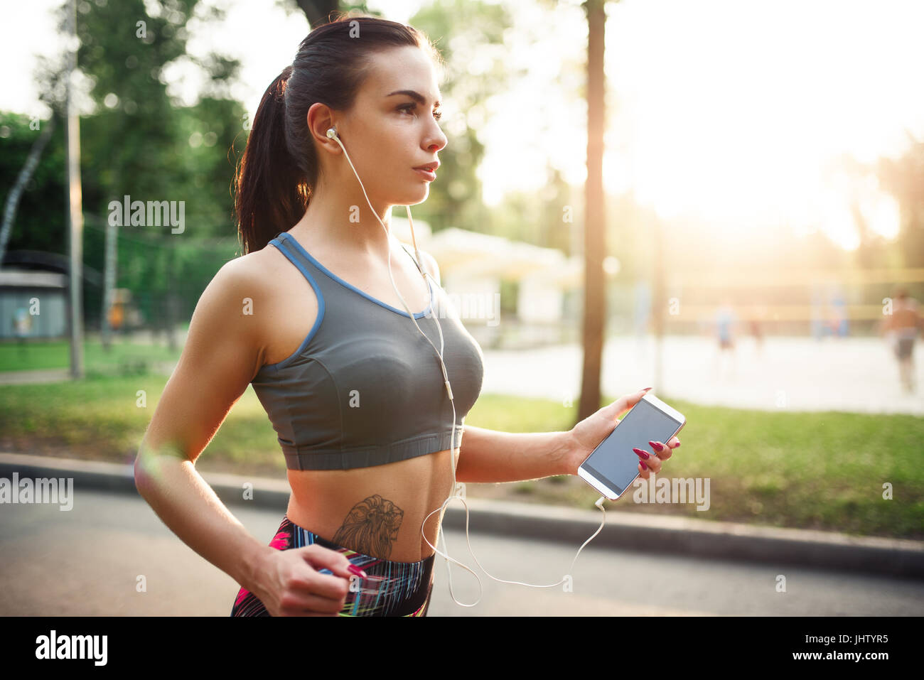 Athletic girl jogging with headphones on walkway in summer park. Woman ...