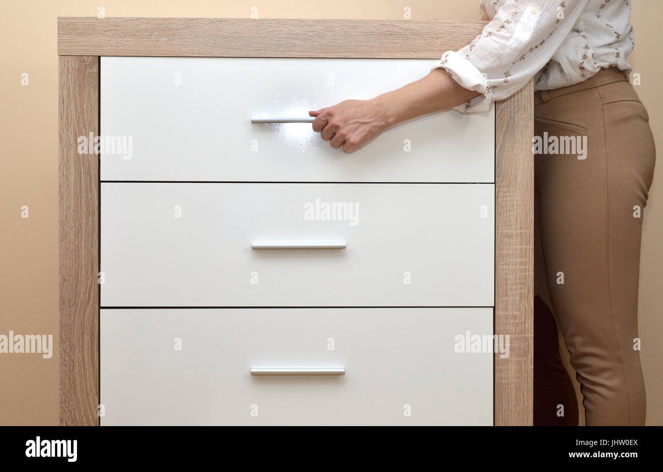 Woman standing beside a dresser holding handle of drawer with her hand ...