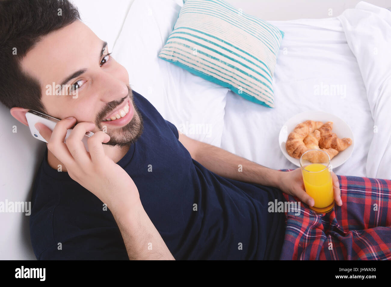 Young man having breakfast and talking on phone in bed. Indoors Stock ...