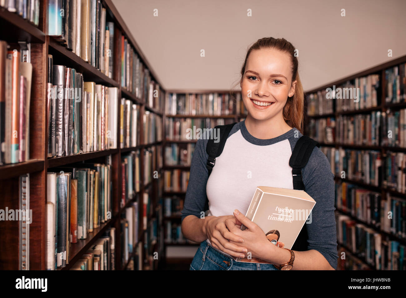 Young caucasian female student standing with a book in library. College ...