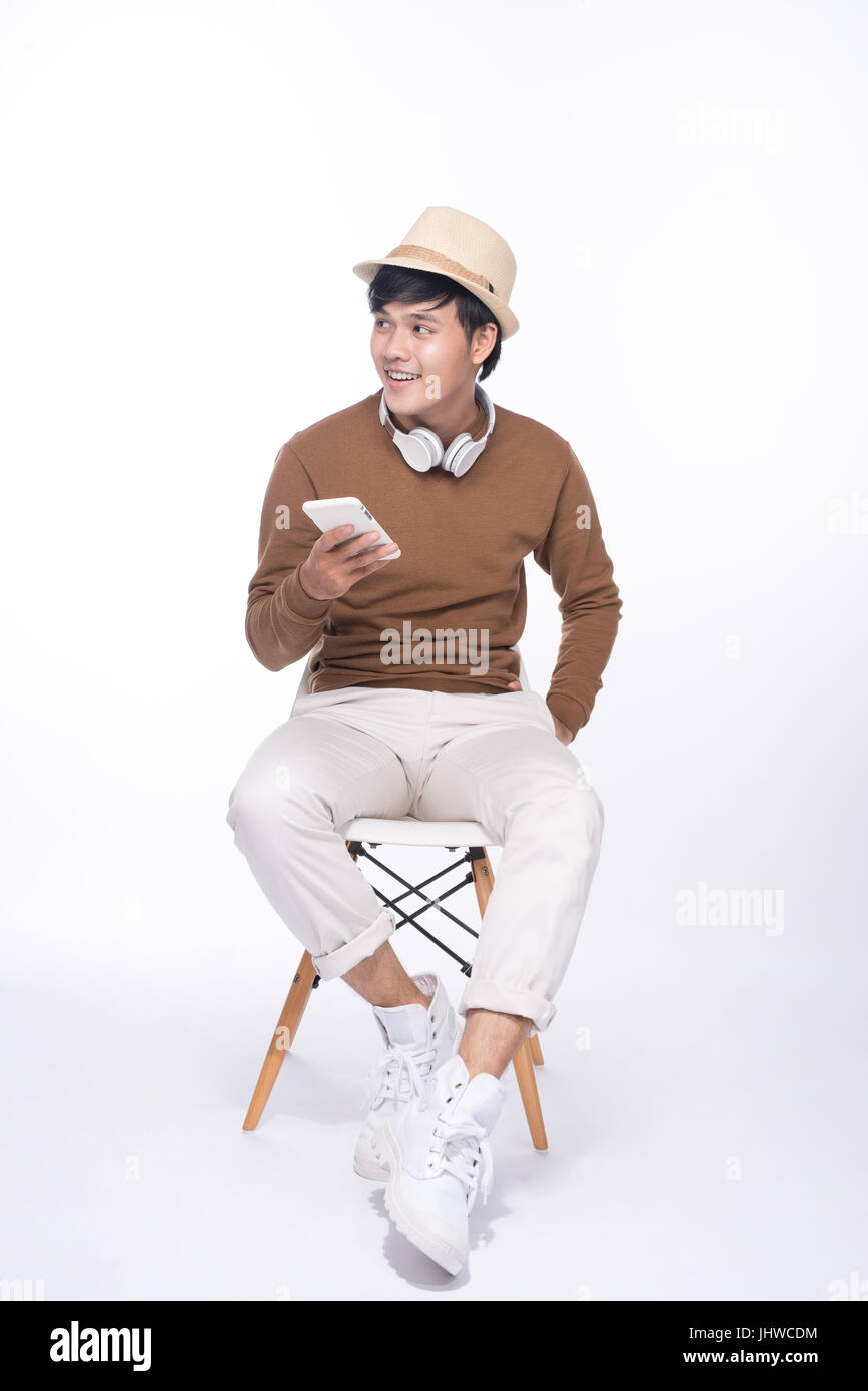 Smart casual asian man seated on chair, holding smartphone in studio ...