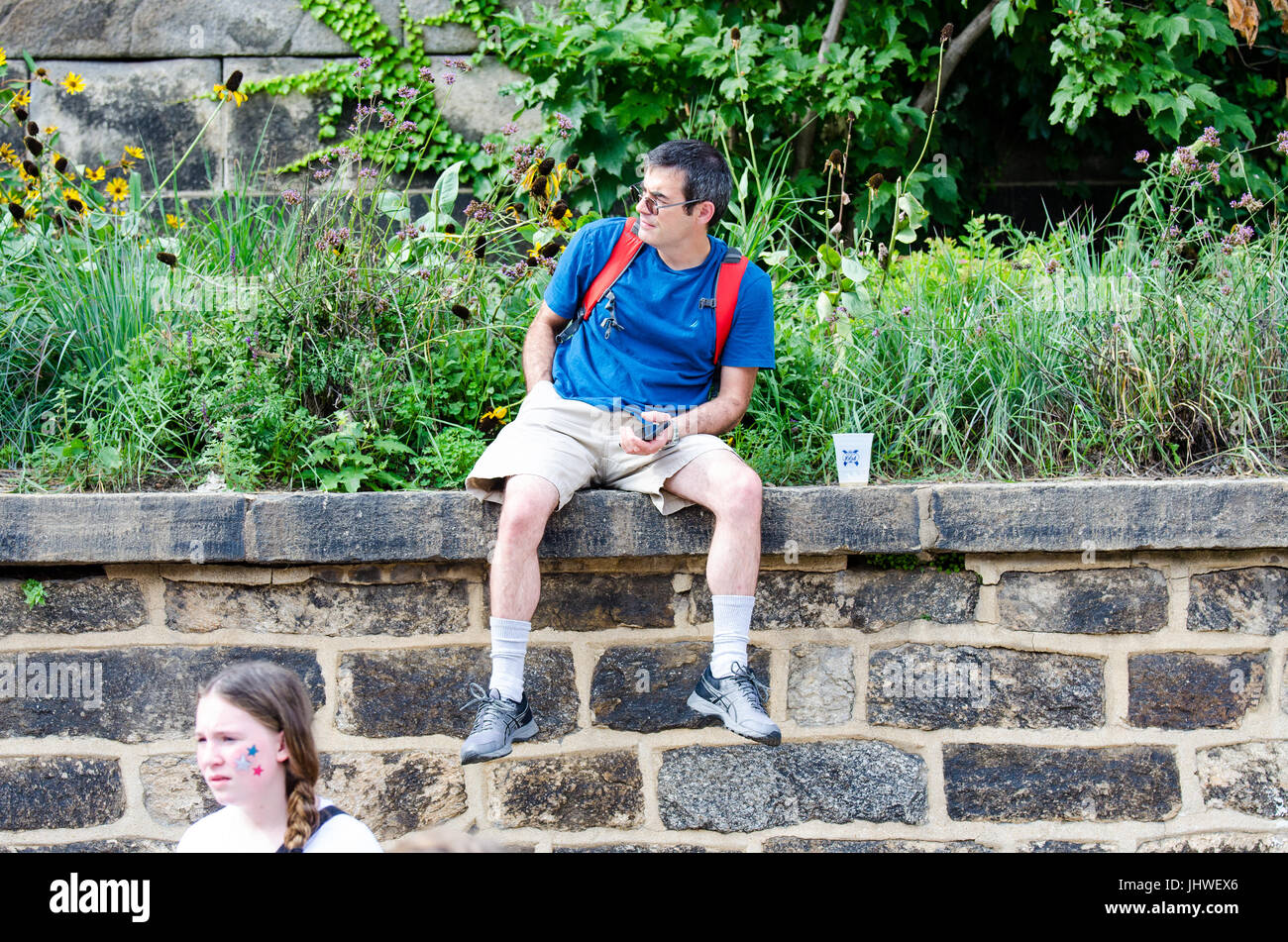 A man sits on a wall watching the crowd Stock Photo - Alamy