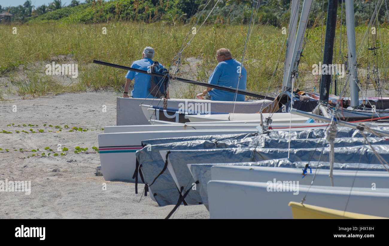 row of empty sailboats with 2 men on a Florida beach Stock Photo - Alamy