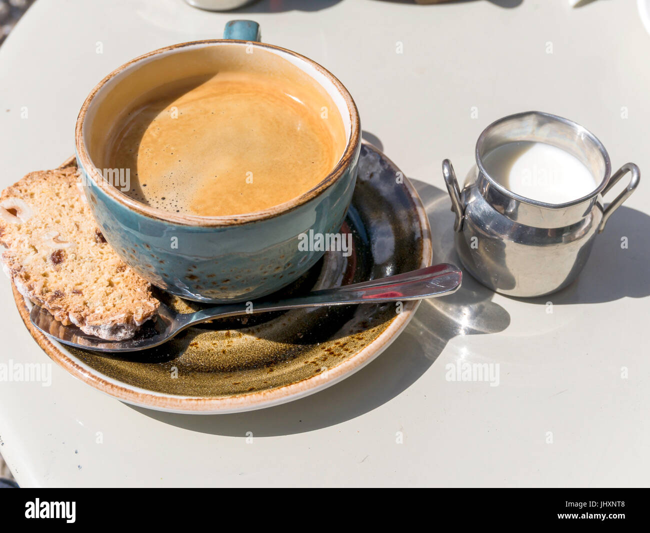 A cup of Americano coffee on an outside café table with a churn of cold ...