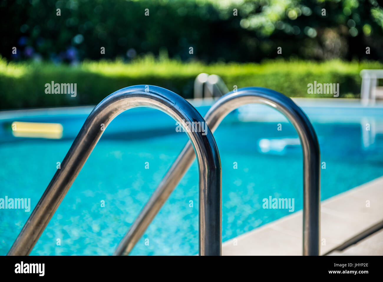 Swimming pool ladder close up, nobody in blue water and green garden ...
