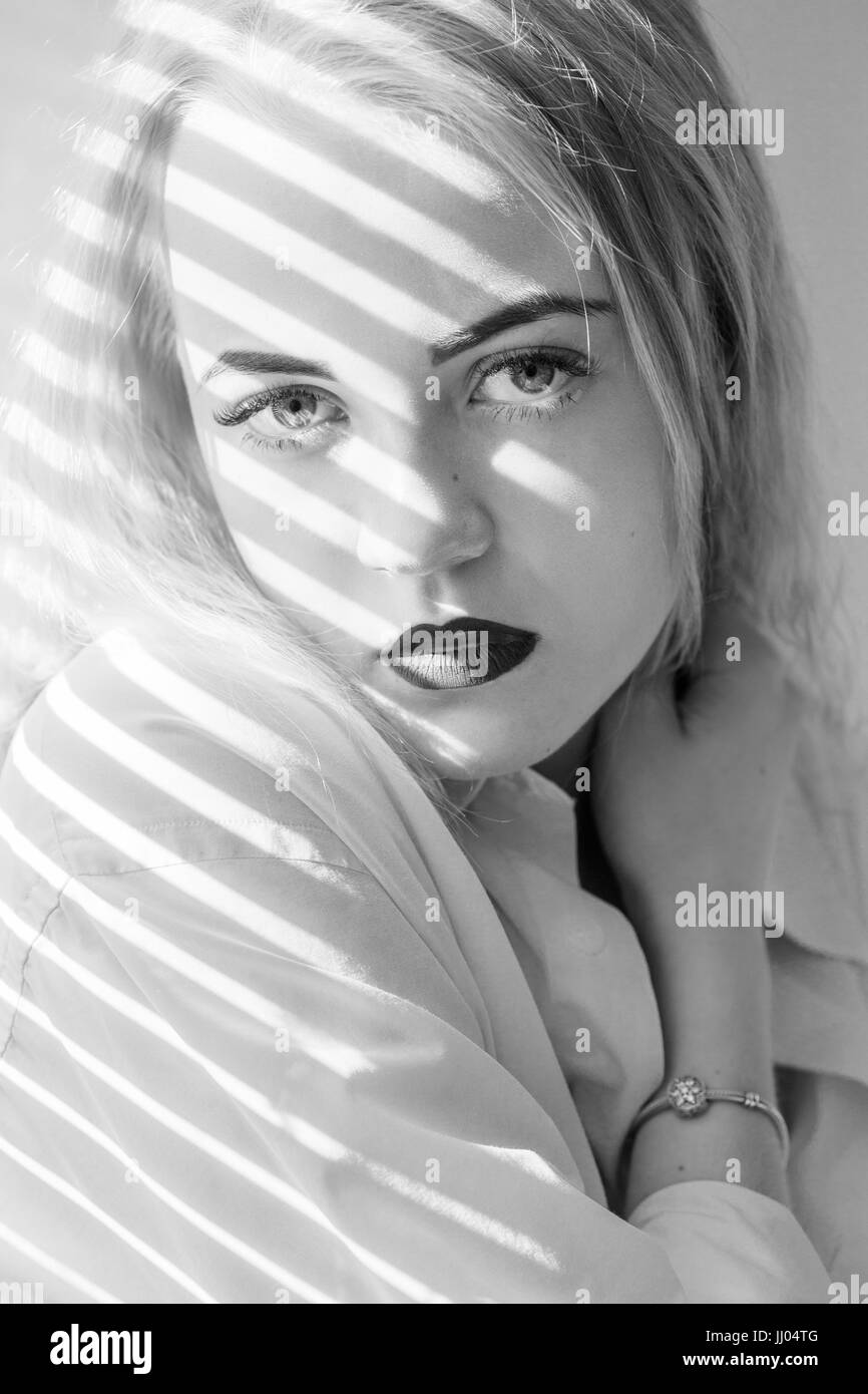 sad girl sitting on window in sunlight with blinds, monochrome Stock ...