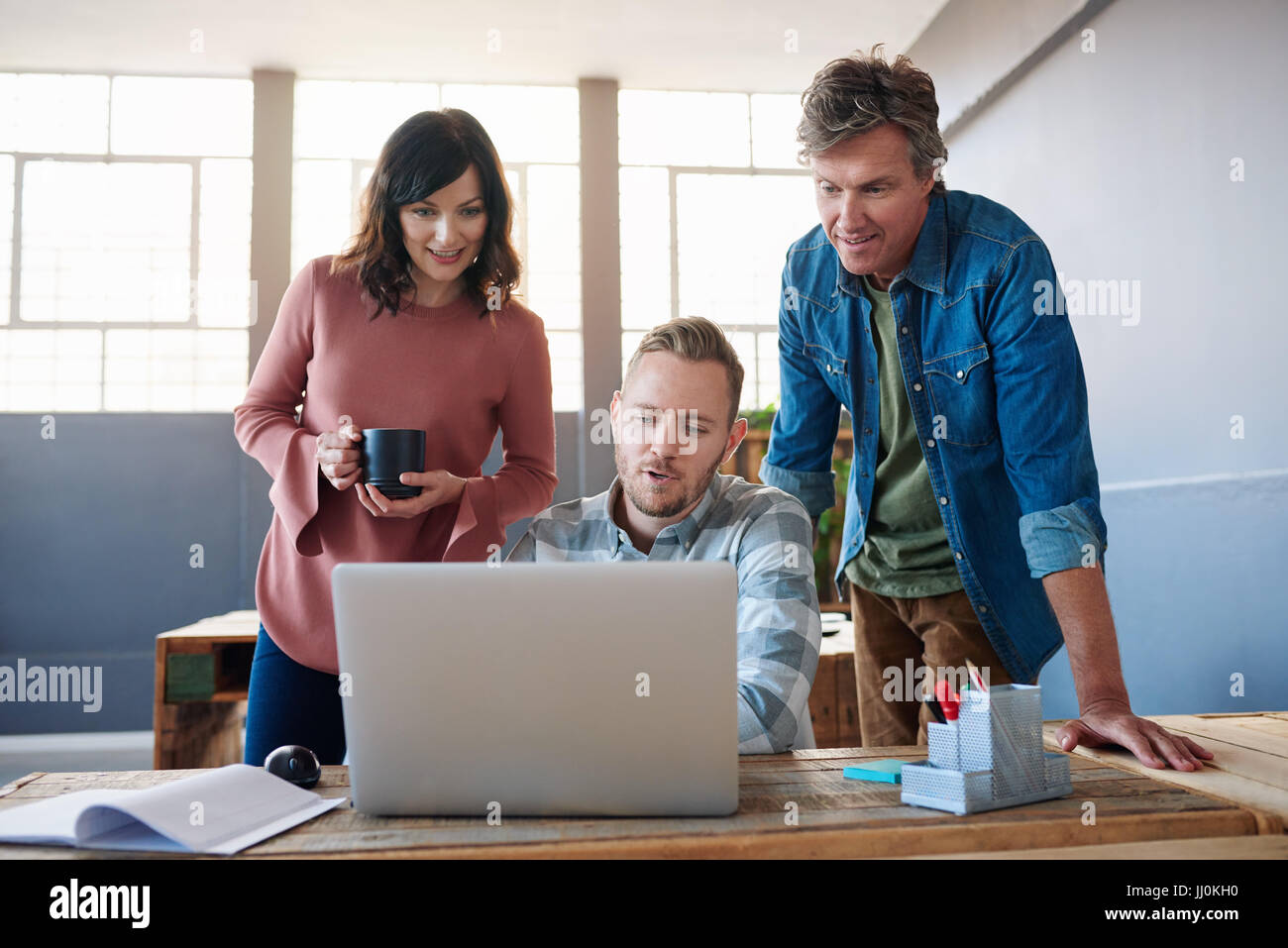 Three coworkers using a laptop together in a modern office Stock Photo ...