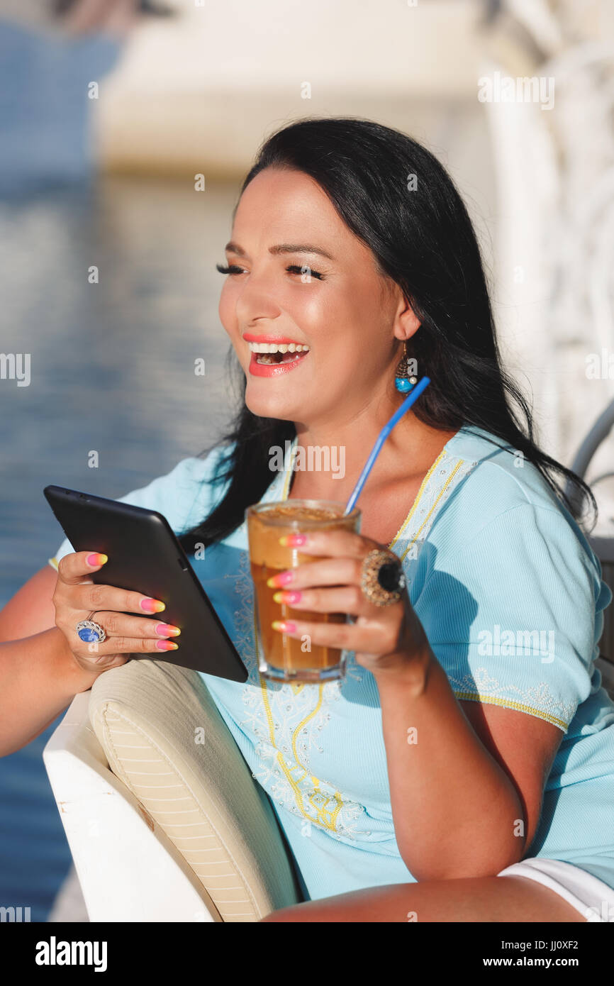Brunette woman sitting in seaside cafe while having coffee and using ...