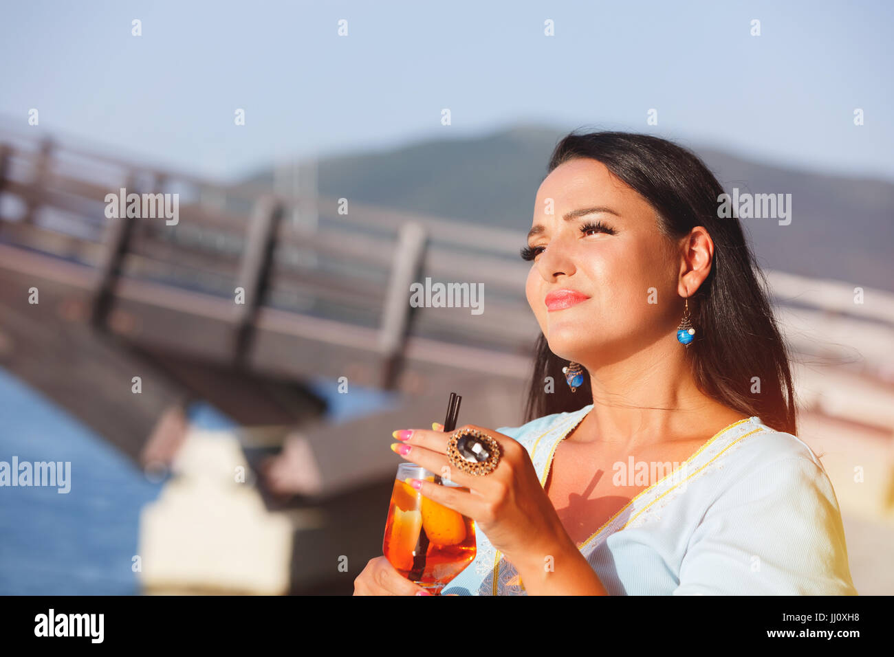 Happy beautiful tanning woman sitting and drinking cocktail in seaside ...