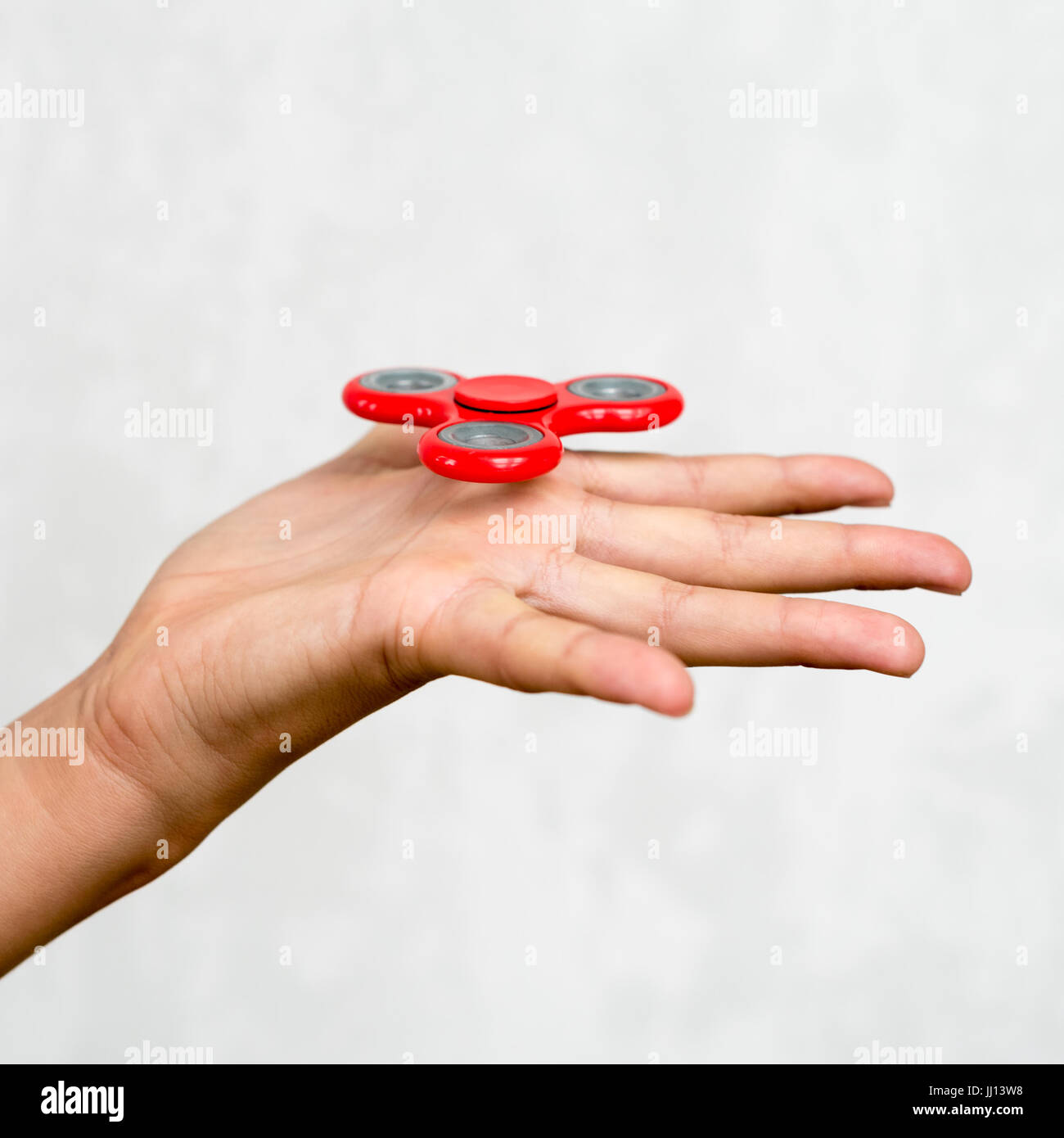 Red hand spinner. Boy playing a popular toy fidget spinner in his hand ...