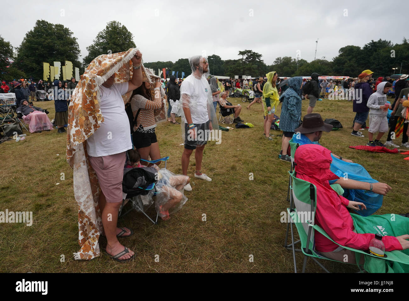 Festival goers protect themselves from the rain while watching a ...