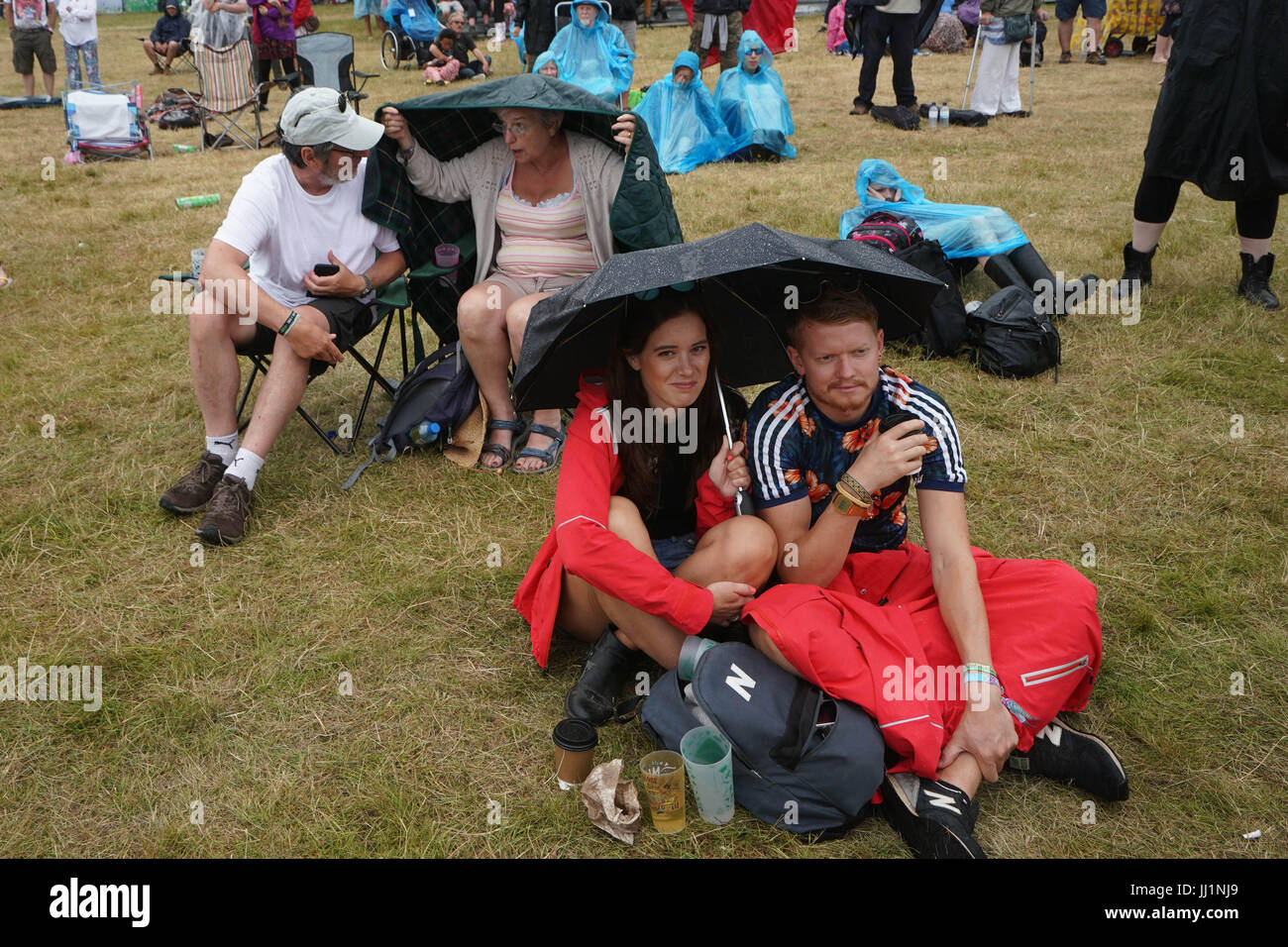 Festival goers protect themselves from the rain while watching a ...