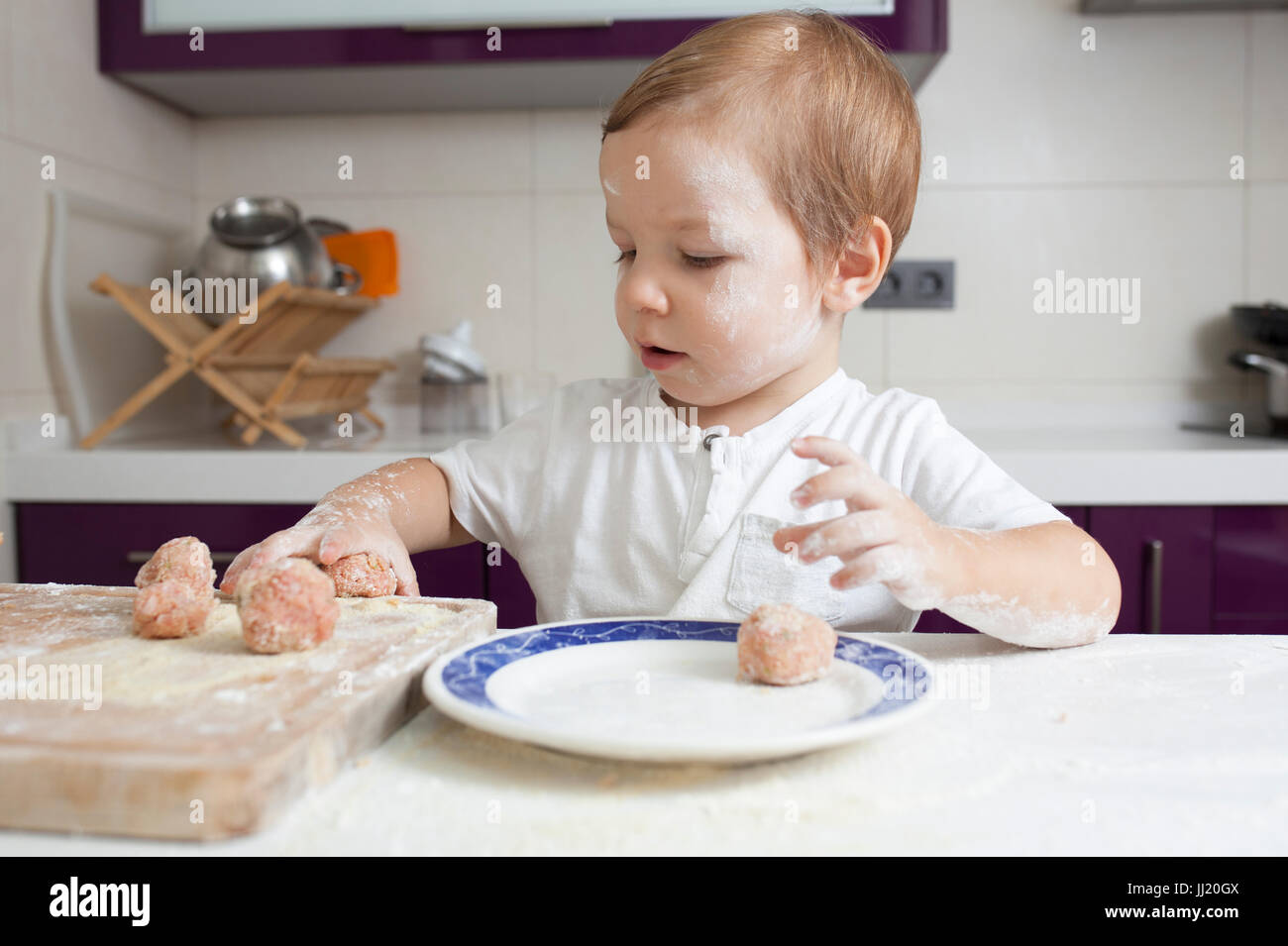 Baby boy preparing meatballs. He is playing with just kneaded meatballs ...