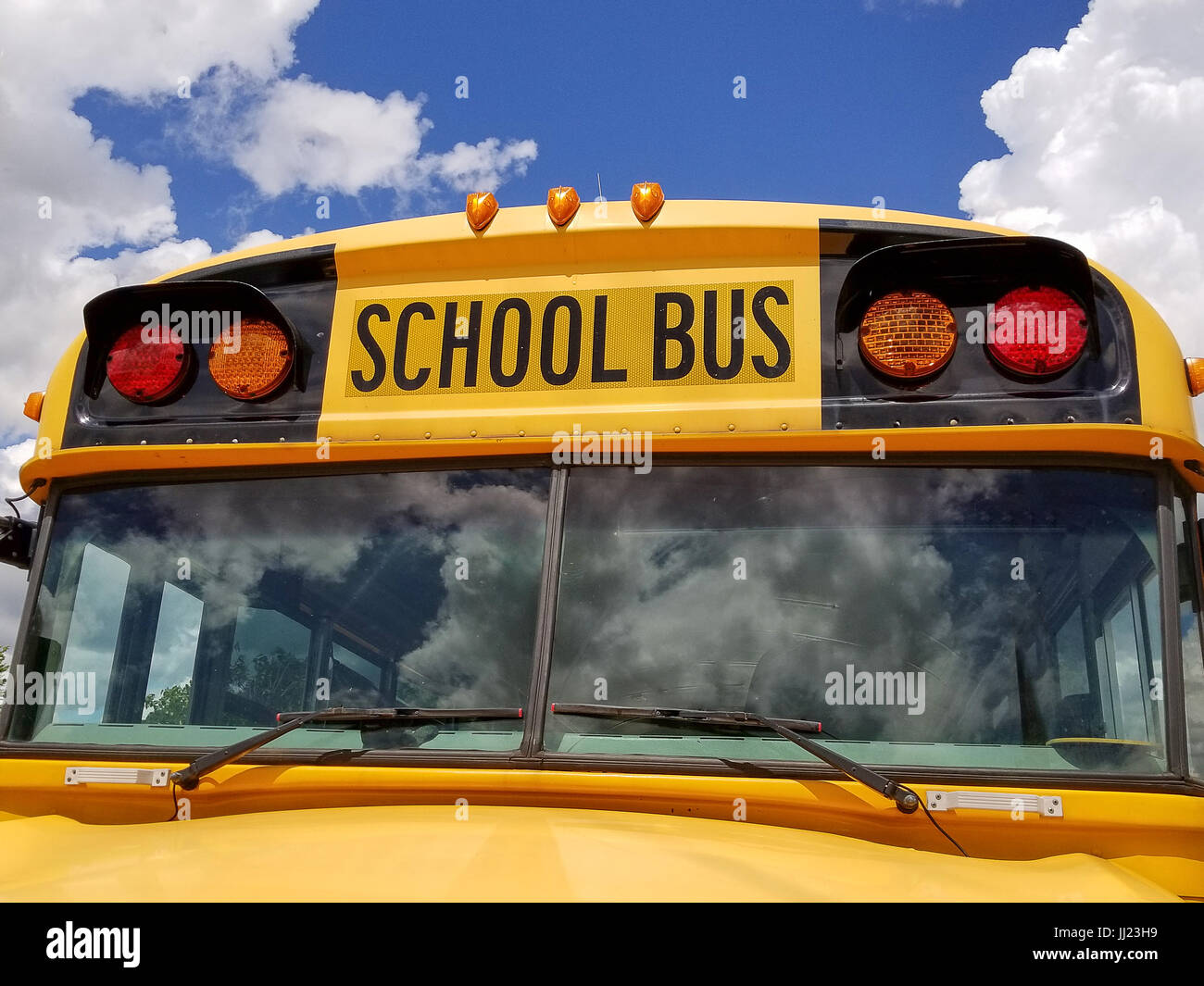 front view of yellow school bus with cloud reflection in windshield ...