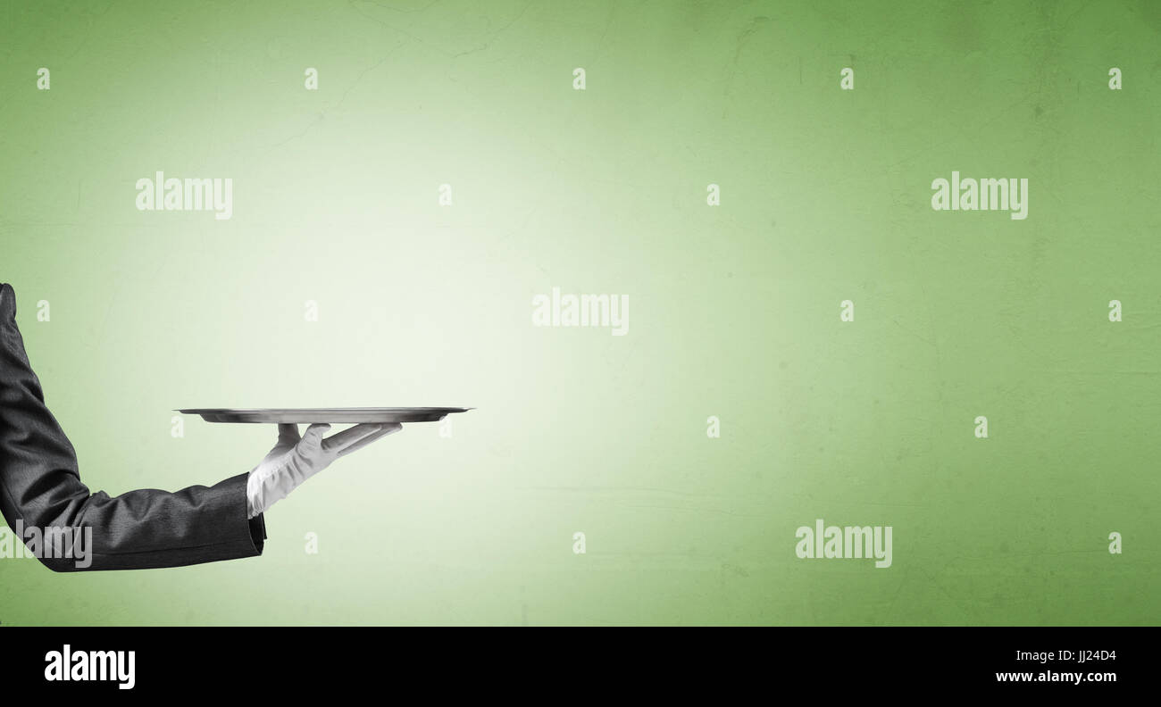 Hand of butler holding empty metal tray against green background Stock ...