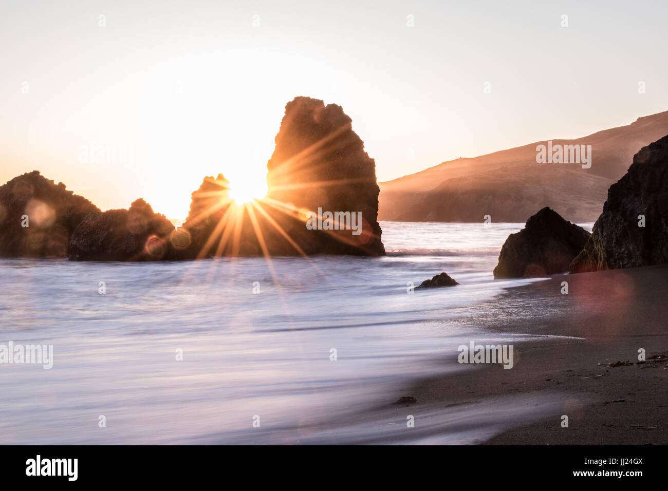 Sunset at the Golden Gate with gold rays splitting two rocks on beach ...
