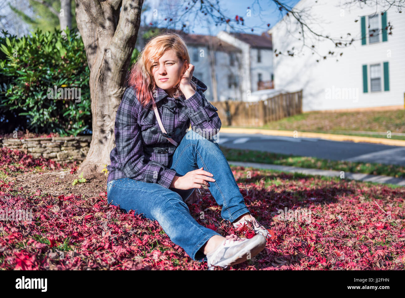 Young woman sitting by tree in autumn red maple leaves foliage in ...