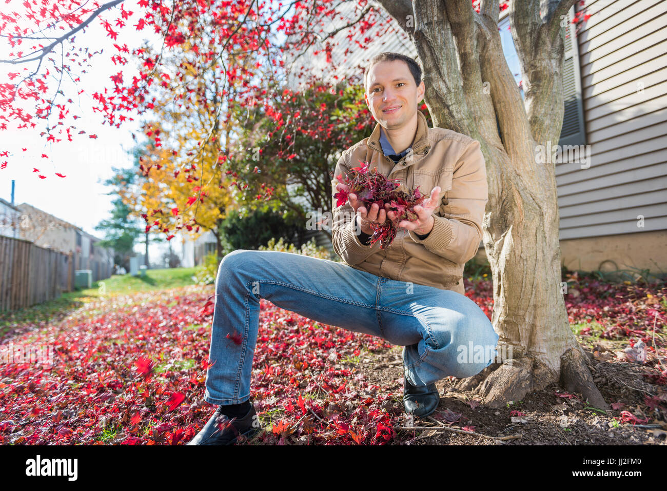 Young man sitting by tree in autumn red maple leaves foliage holding ...