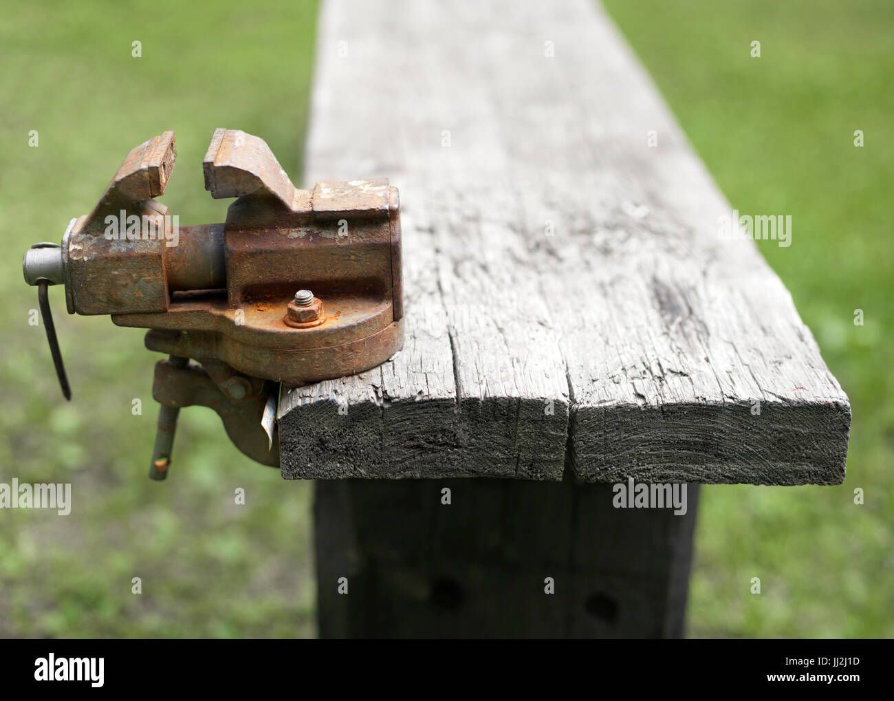 Abandoned rusty clamp attached to a wooden bench. Outdoor cropped shot ...