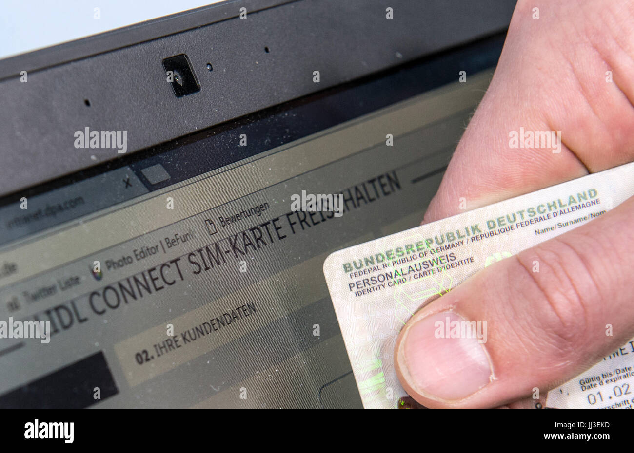 A man holds his German ID card in front of the camera of a laptop ...