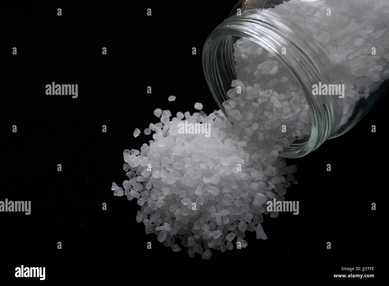 closeup of a small sea salt crystals pile spilled from small jar ...