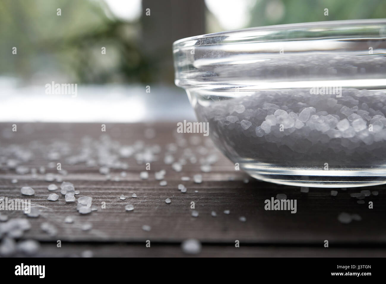 white sea salt in glass bowl on dark wooden kitchen table scattered ...