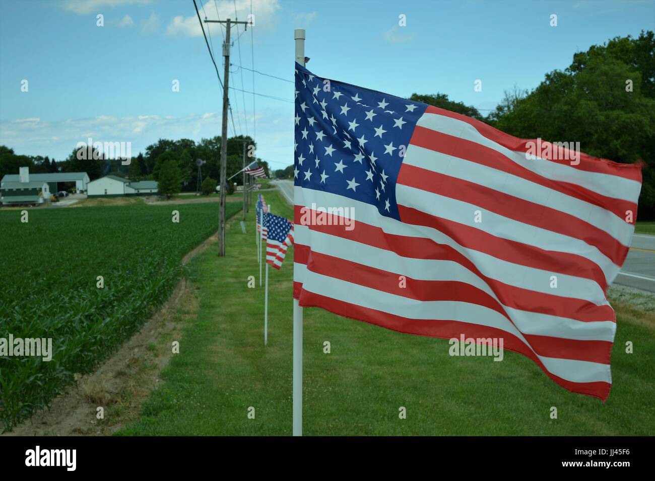 American flag flying along side fo country 2 lane road with corn in ...
