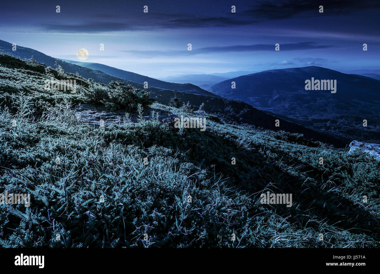 grassy meadow on hillside of mountain ridge at night in full moon light ...