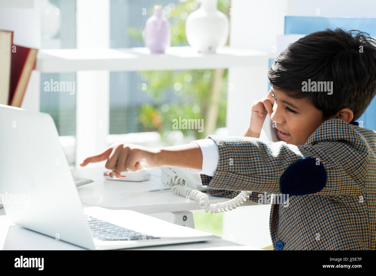 Profile view of businessman using telephone while pointing on laptop at ...