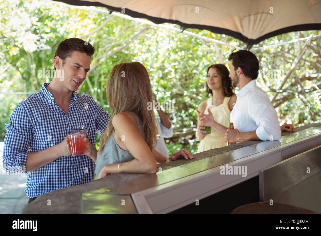 Smiling friends interacting while having a cocktail at counter in ...