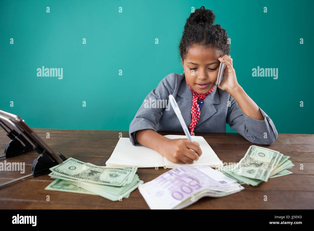 Businesswoman using phone while writing on book by paper currency at ...