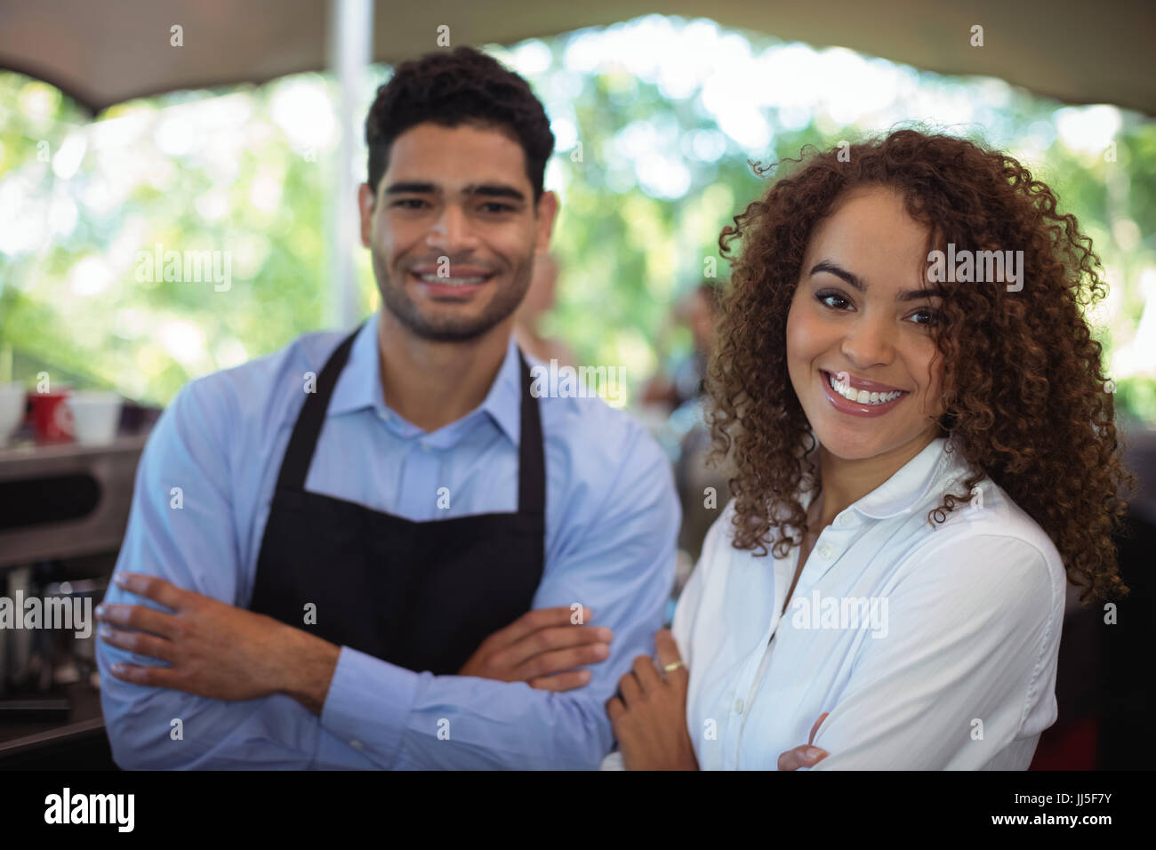 Portrait of smiling waiter and waitress standing with arms crossed at ...