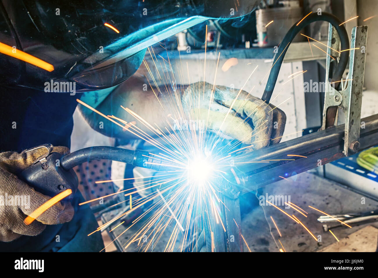 A close-up man is weld metal with a welding machine, blue sparks fly to ...