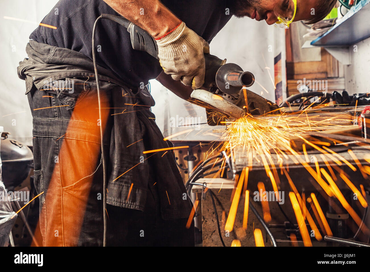 A young man is cooking metal with a welding machine, blue sparks fly to ...
