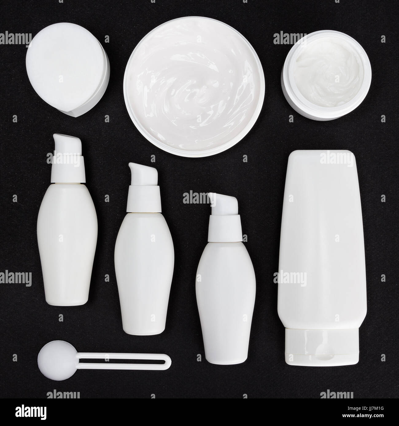 White cosmetic containers on black surface. Different cosmetic products ...