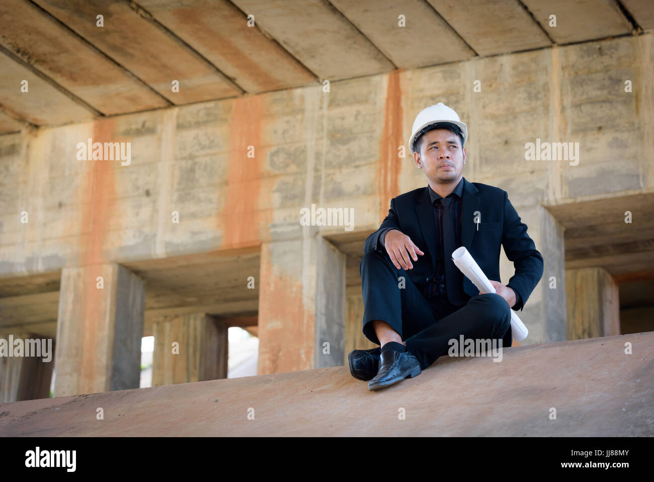 Construction engineer sits tired under the bridge Stock Photo - Alamy