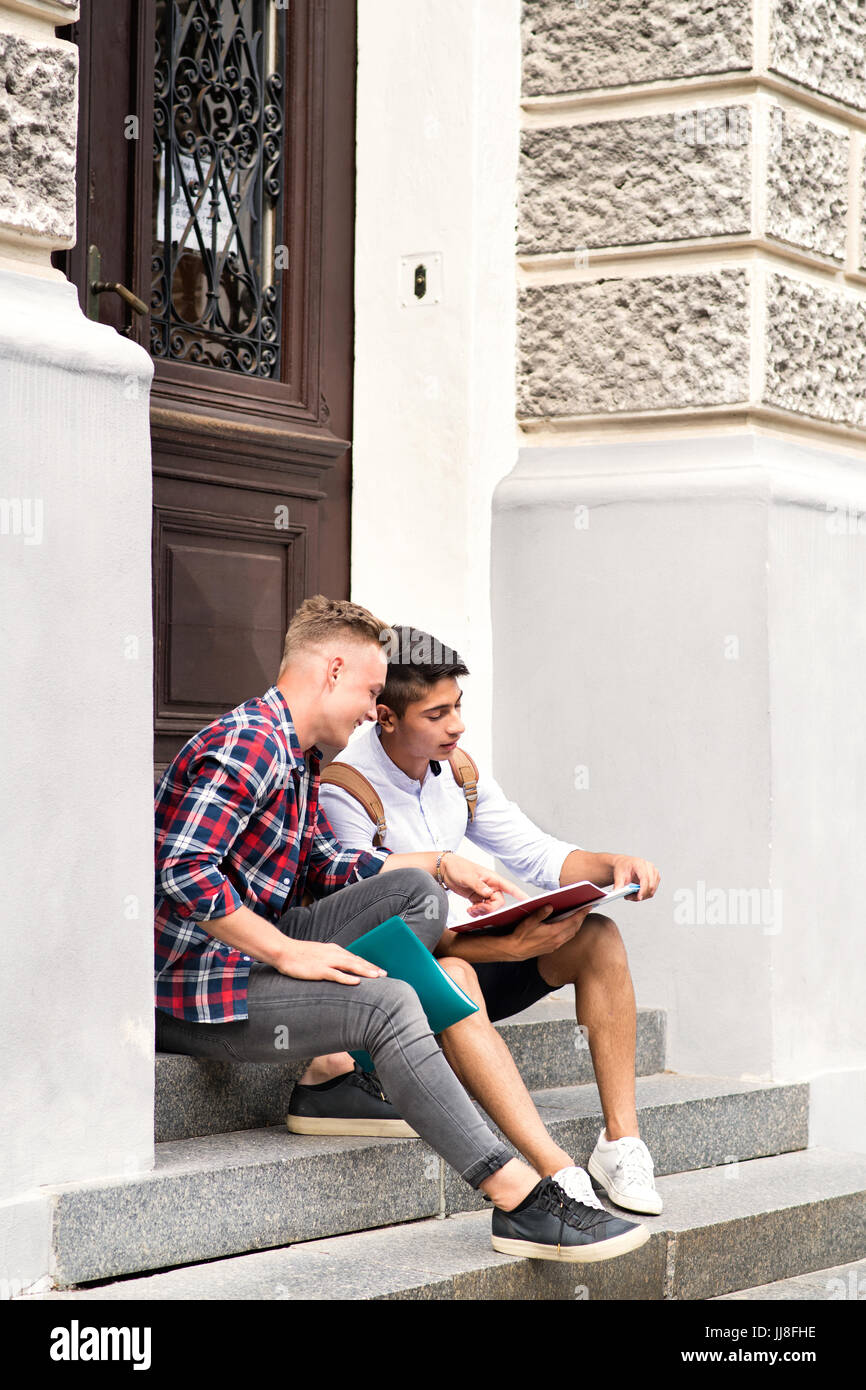 Teenage students sitting on stone steps in front of university Stock ...