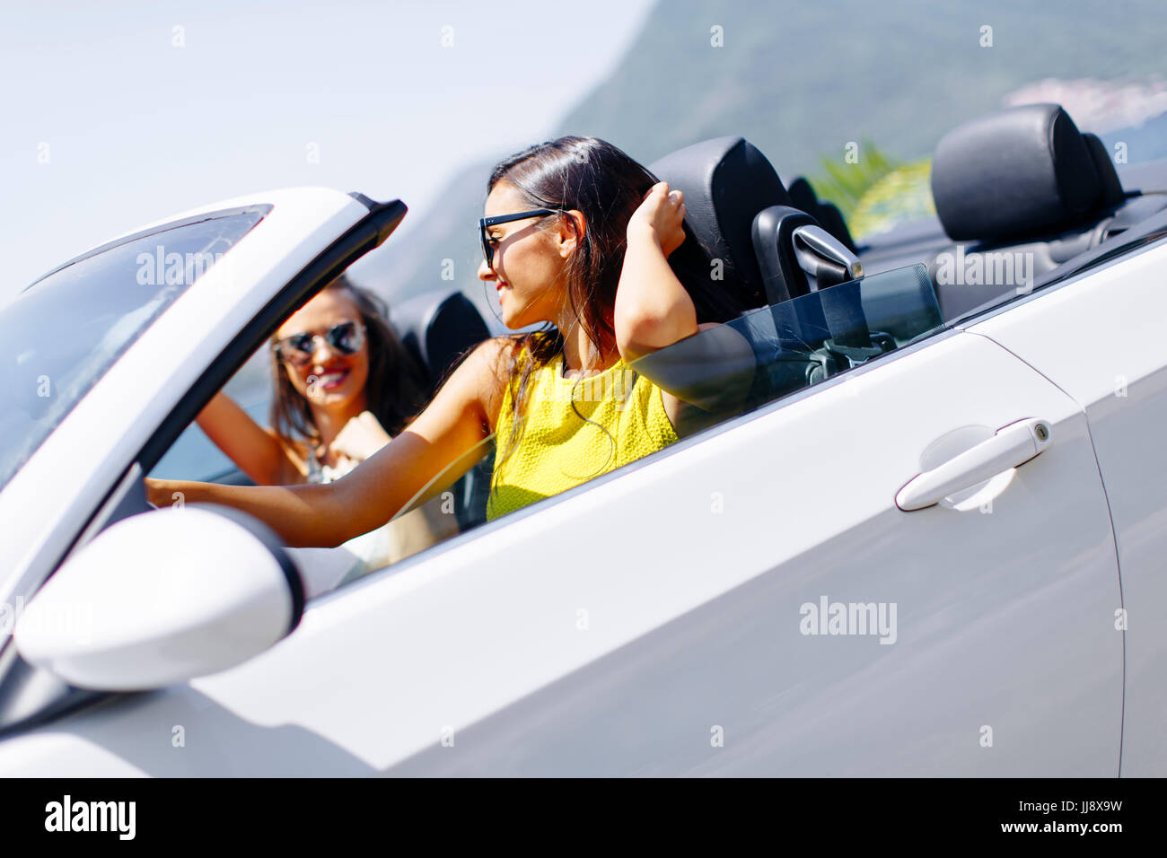 Two happy friends in white cabriolet car driving everywhere and looking ...