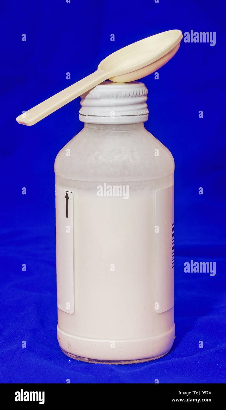 White bottle with medical drug syrup and a small spoon, blue background ...