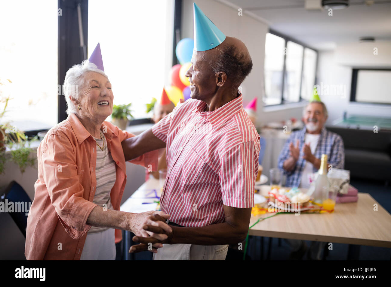 Senior couple wearing party hats dancing at birthday party in nursing ...