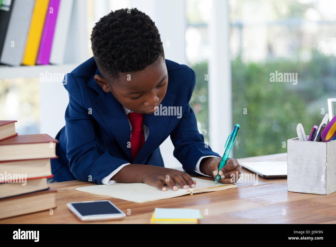 Boy imitating as businessman writing on diary at desk in office Stock ...