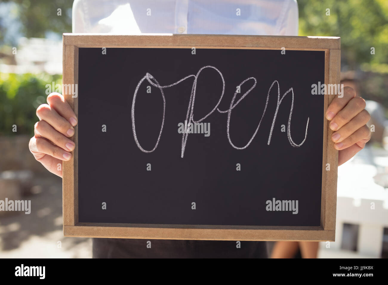 Mid section of waitress standing with open sign board in restaurant ...