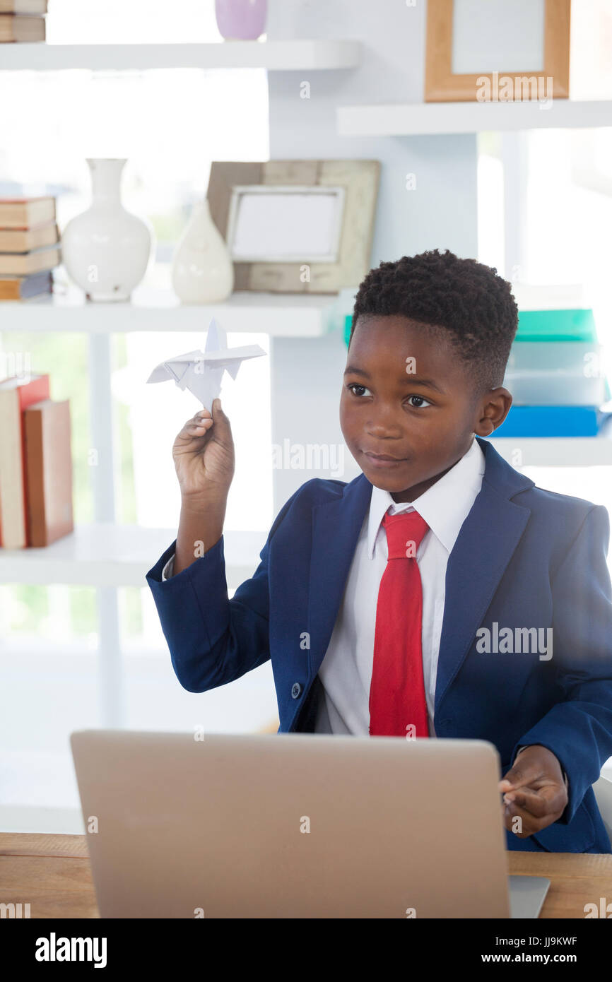 Boy imitating as businessman playing with paper airplane while sitting ...