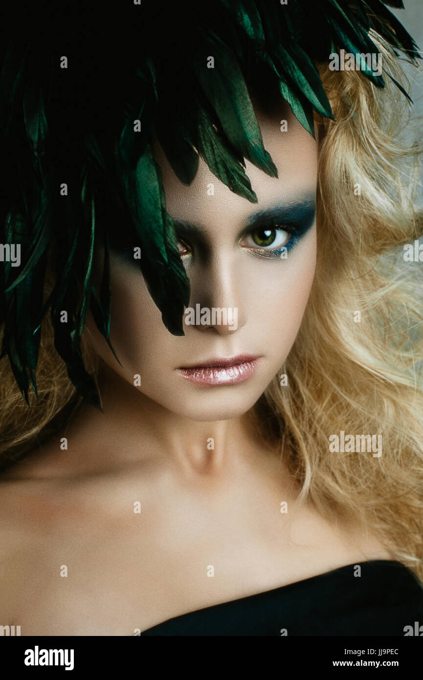 Beautiful girl in the image of a bird posing with feathers with bright ...
